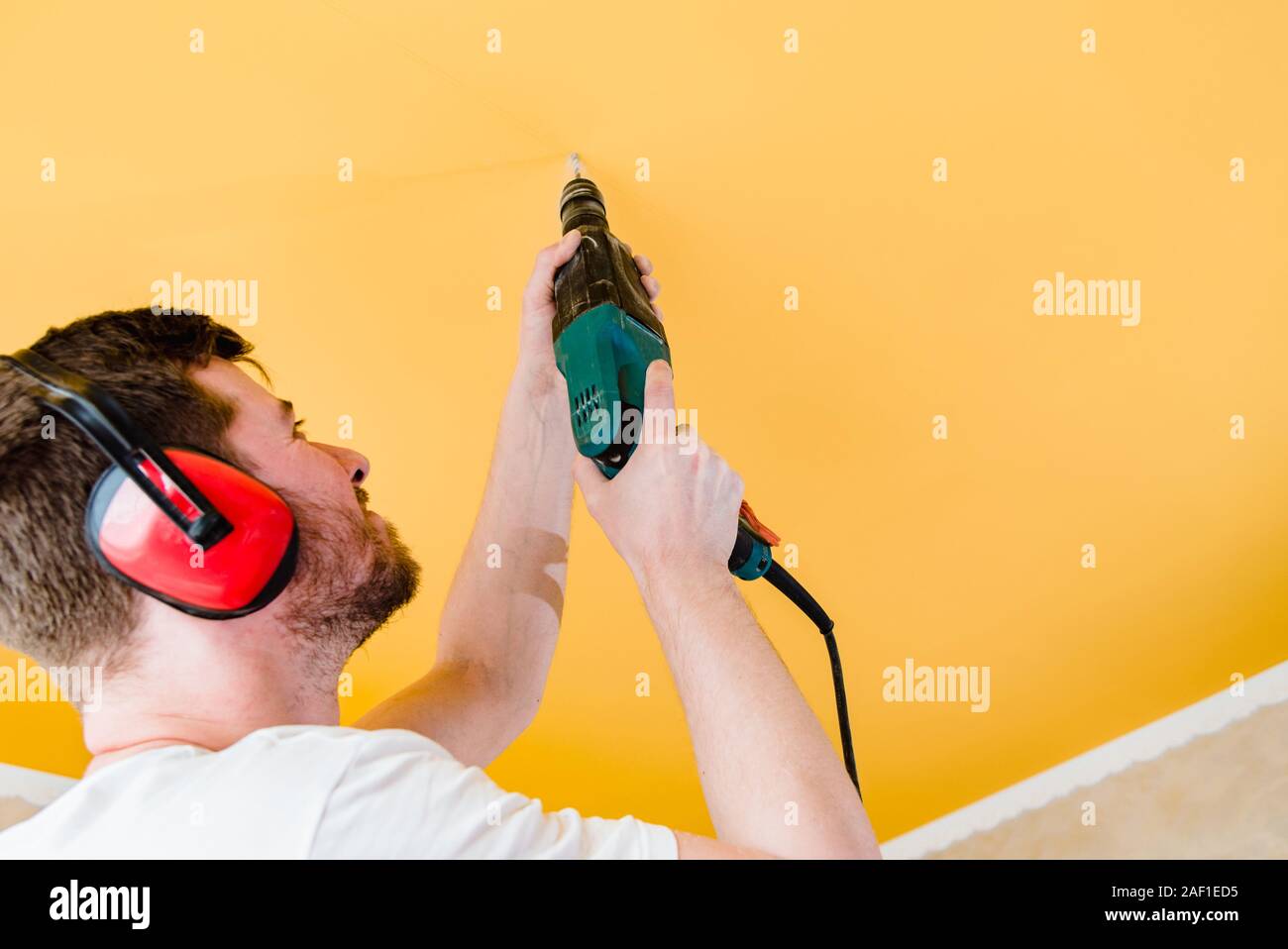 the guy is drilling a hole in the ceiling with a drill in his apartment ...