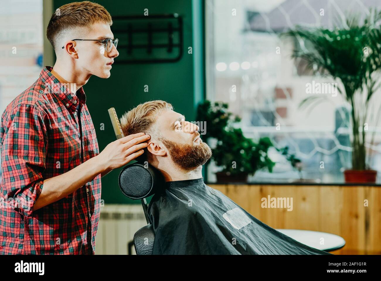 young guy hairdresser cuts beard to man in salon Stock Photo - Alamy