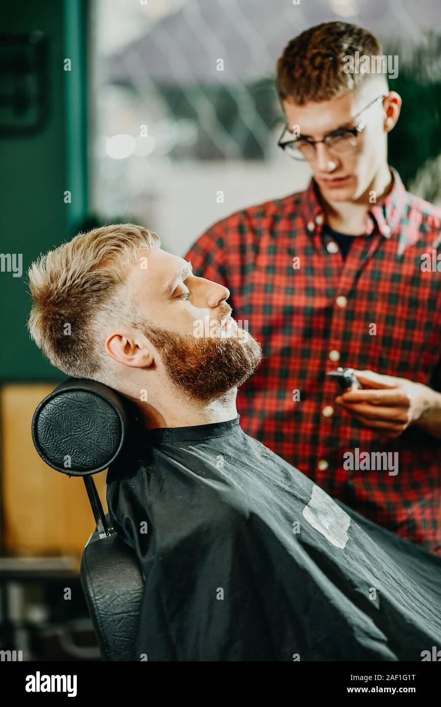 young guy hairdresser cuts beard to man in salon Stock Photo - Alamy