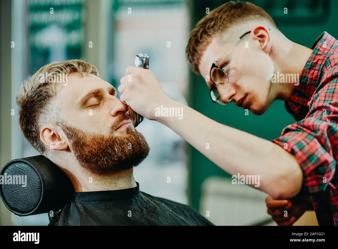 young guy hairdresser cuts beard to man in salon Stock Photo - Alamy