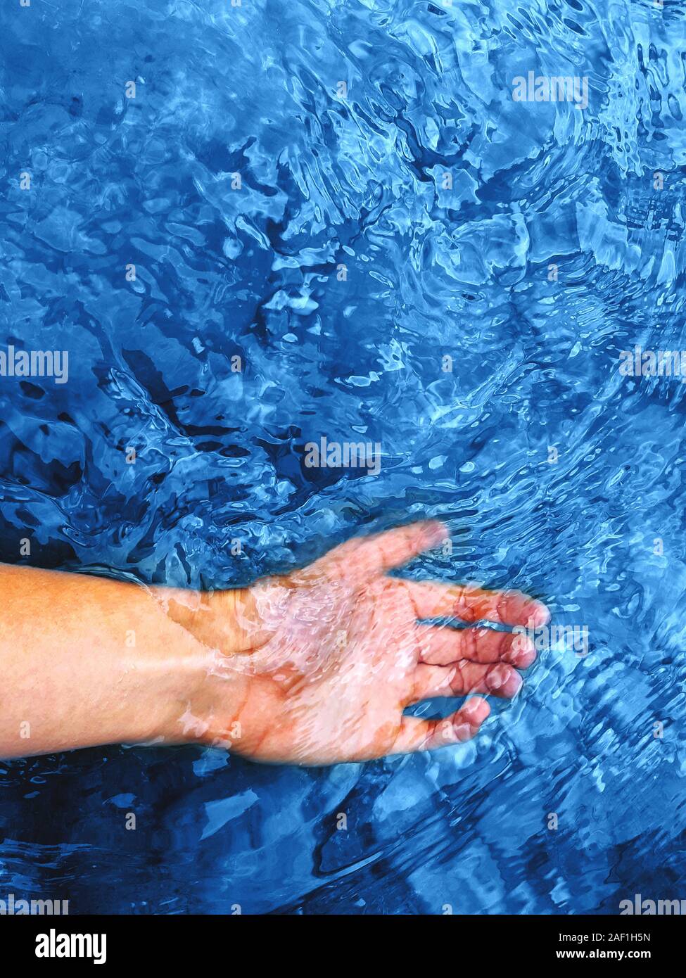 Classic blue color of 2020. Water surface with ripples and female hand ...