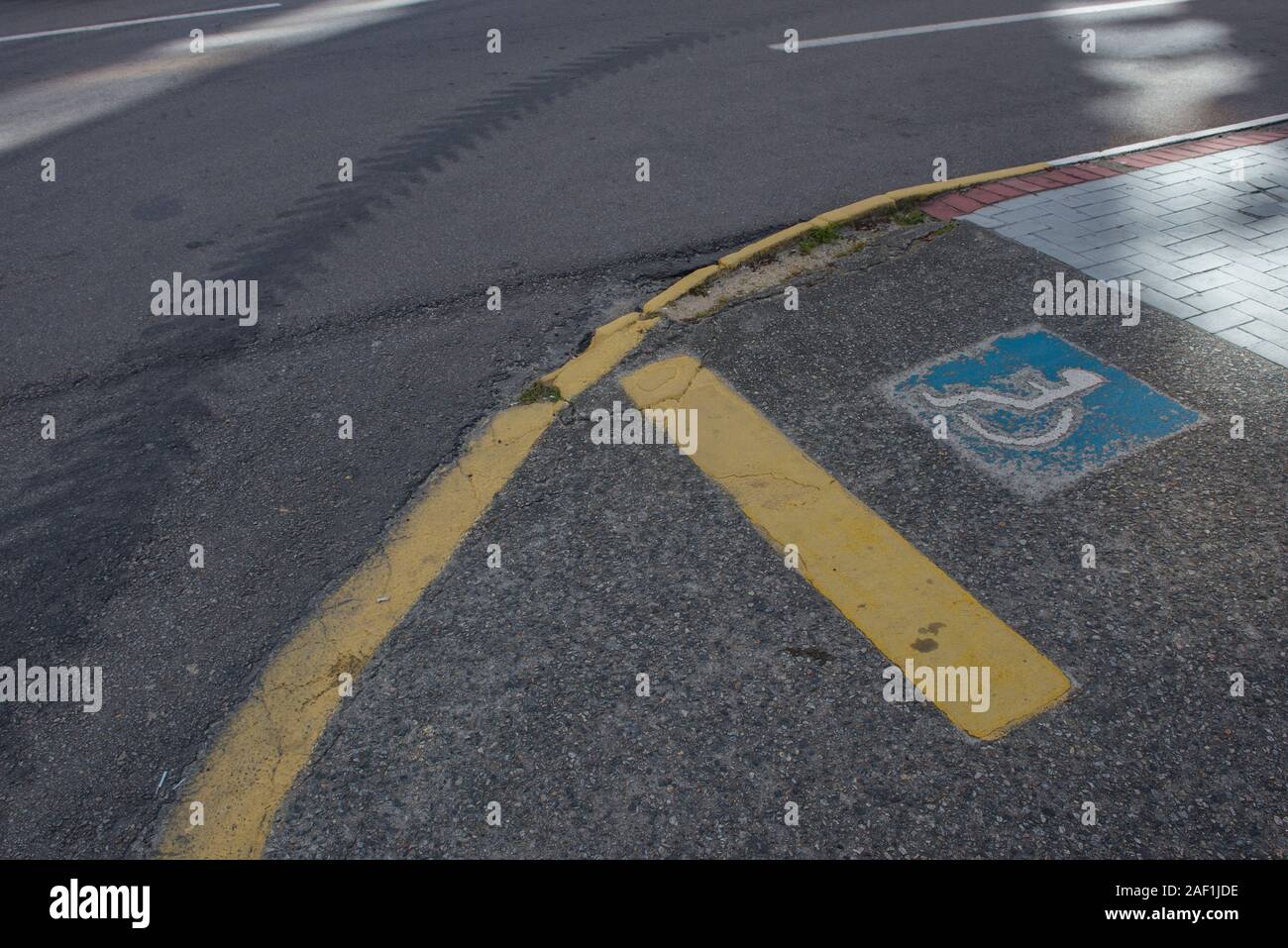 Wheelchair users symbol in a sidewalk, and tire marks on street corner ...