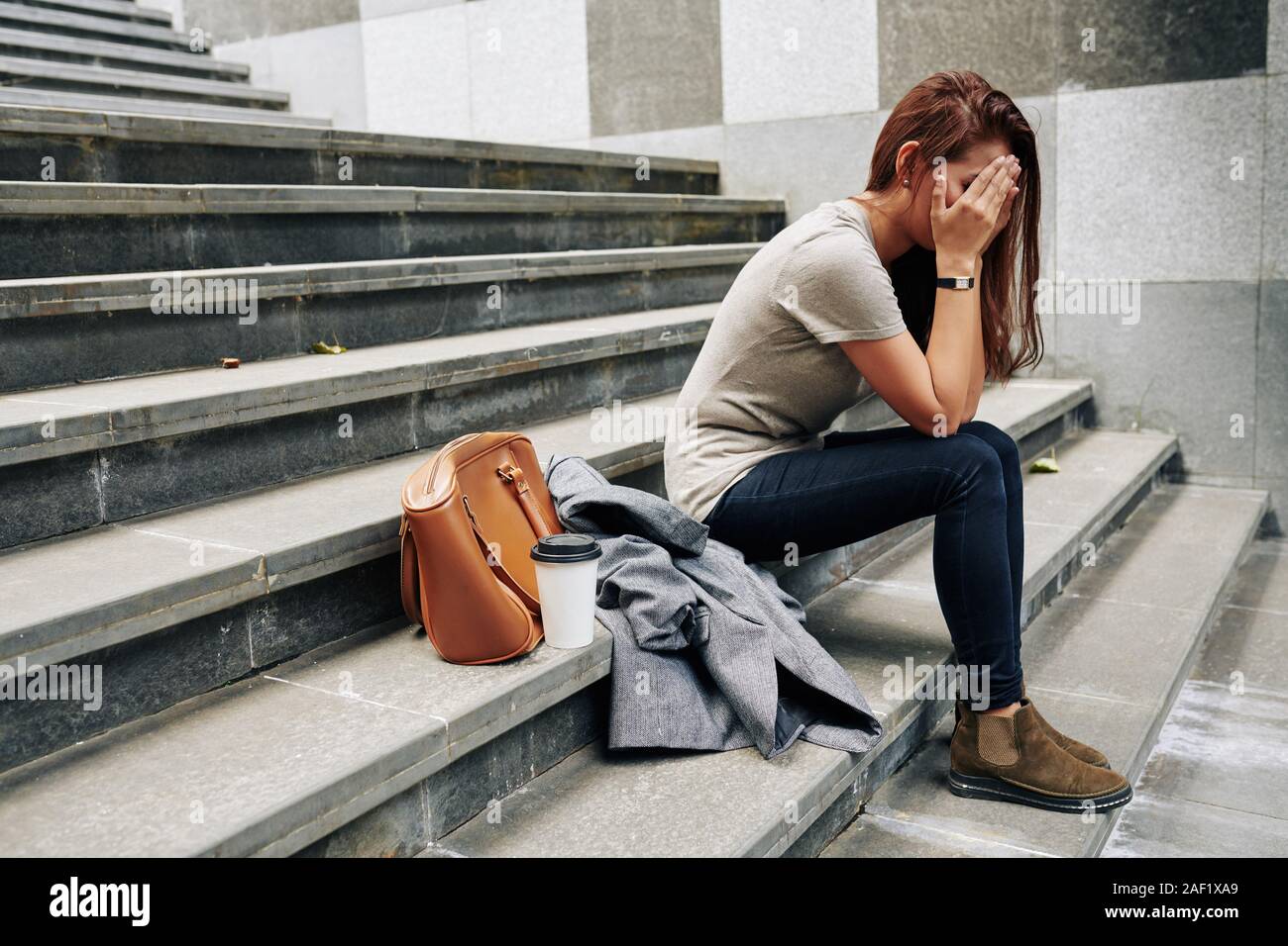 Pretty young woman sitting on steps outdoor and covering face when ...