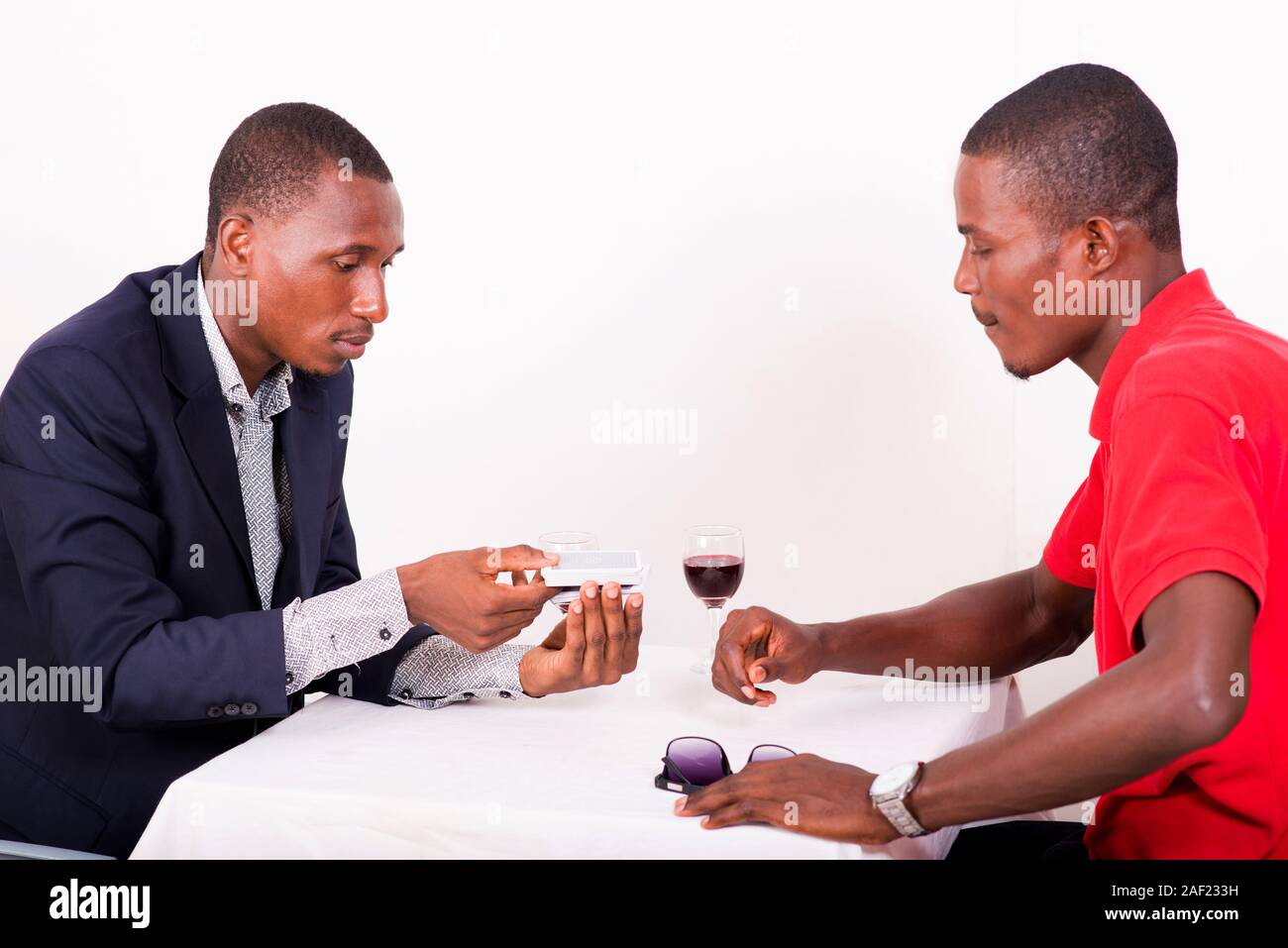 two young men playing cards and sitting around a table while drinking ...