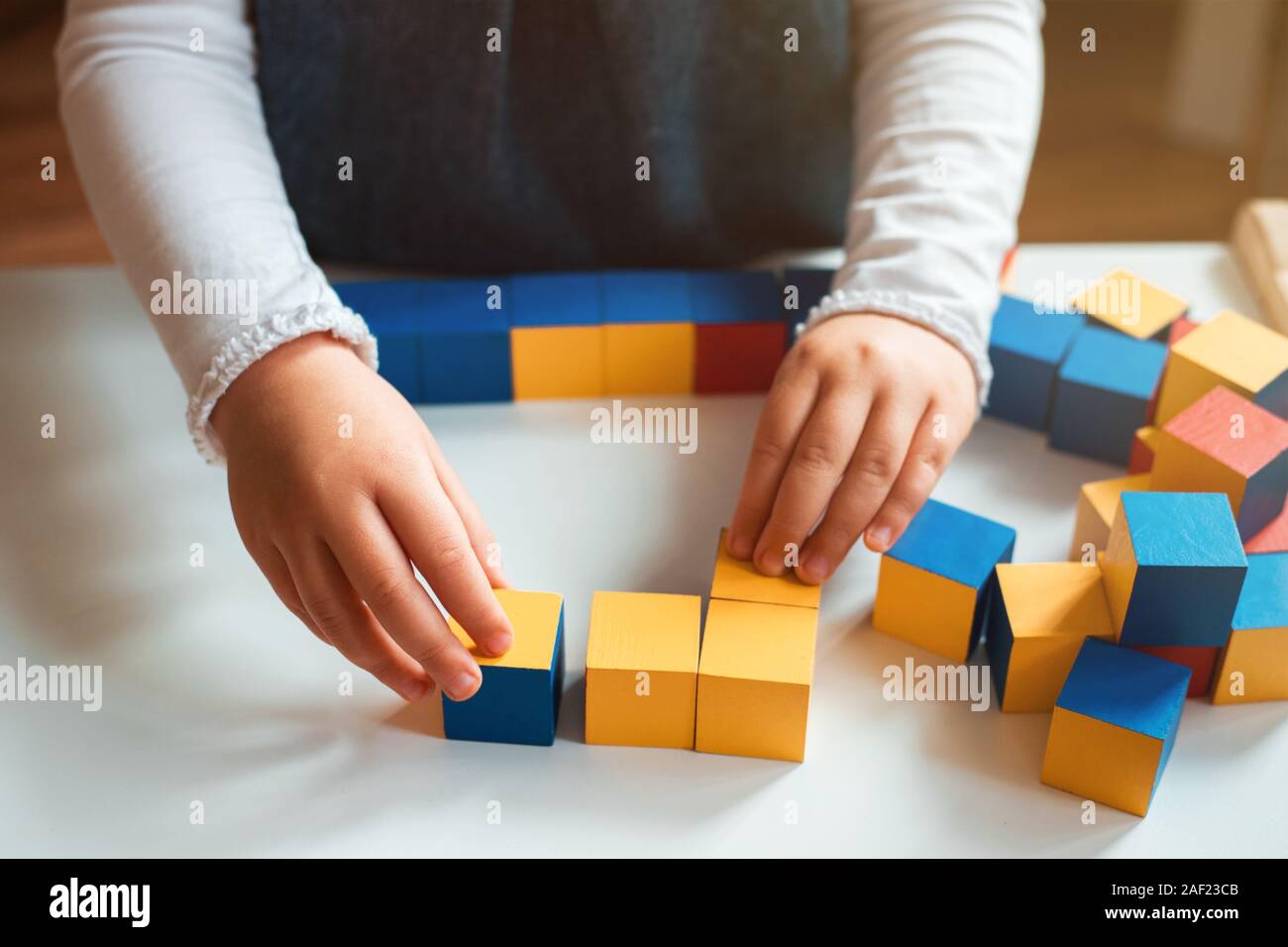 Little girl playing with colorful wooden bricks at home. She builds ...