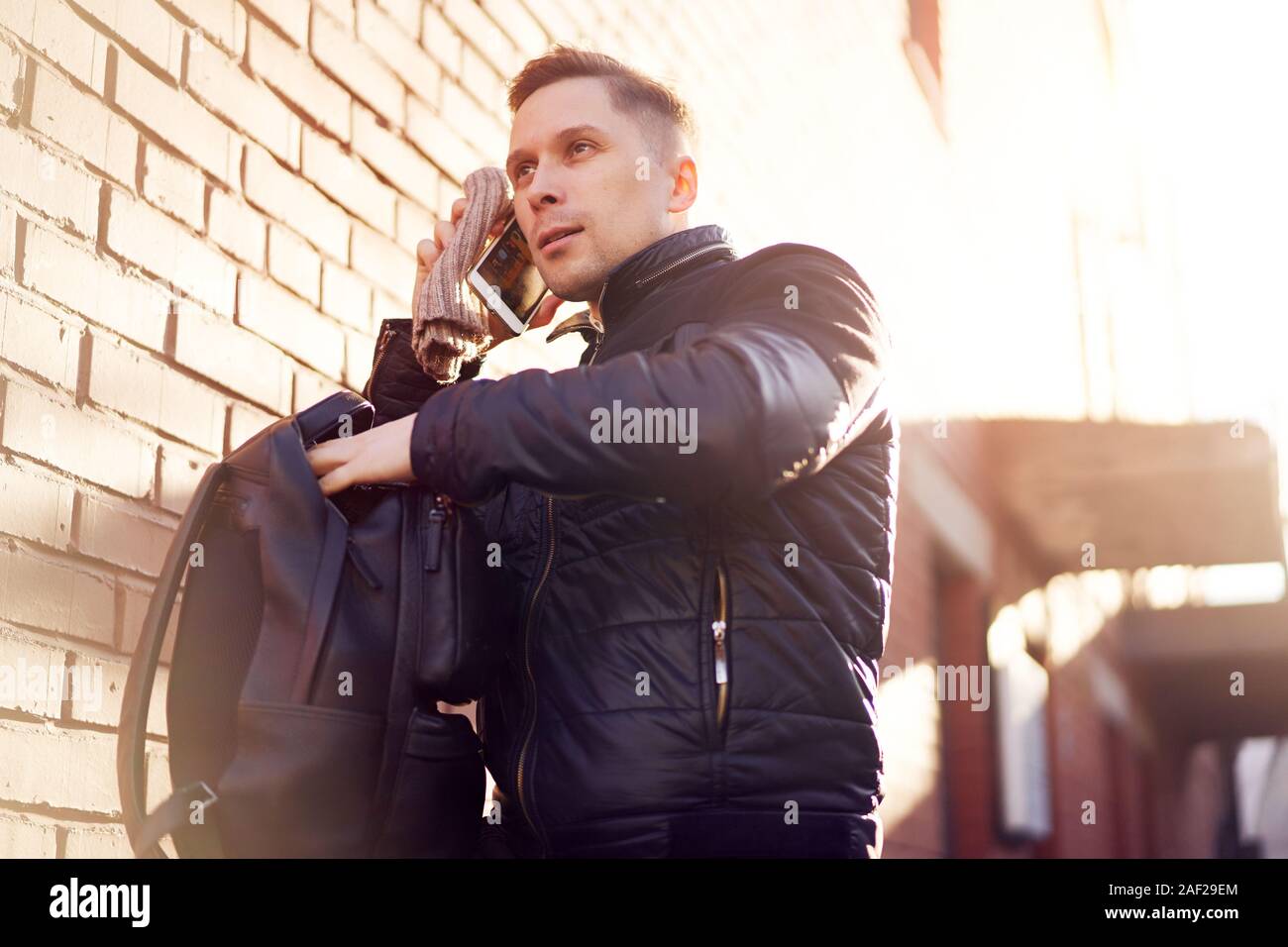 Male looking at side talking on phone while standing by brick modern ...