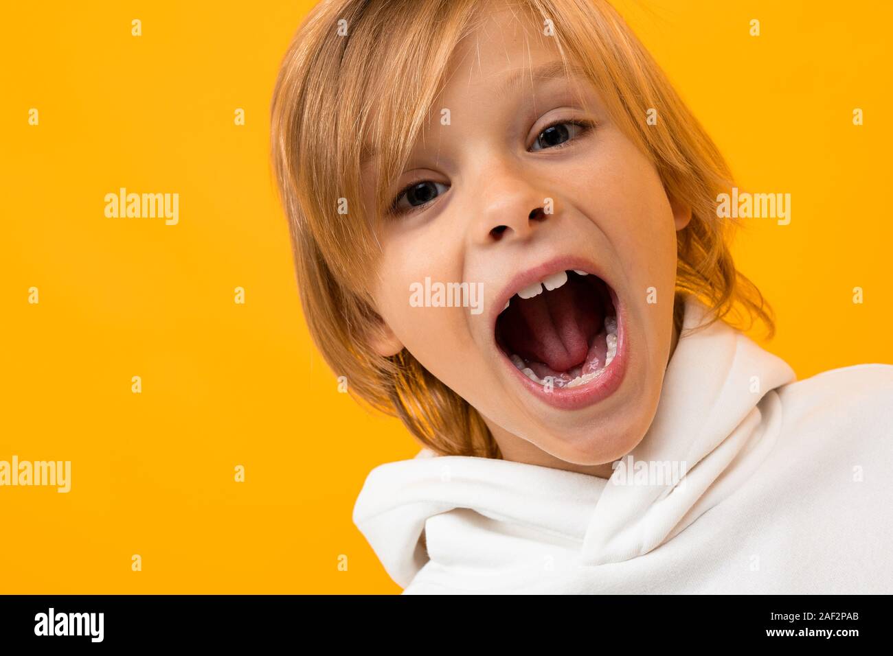 cute blond boy screams on a yellow studio background close-up Stock ...