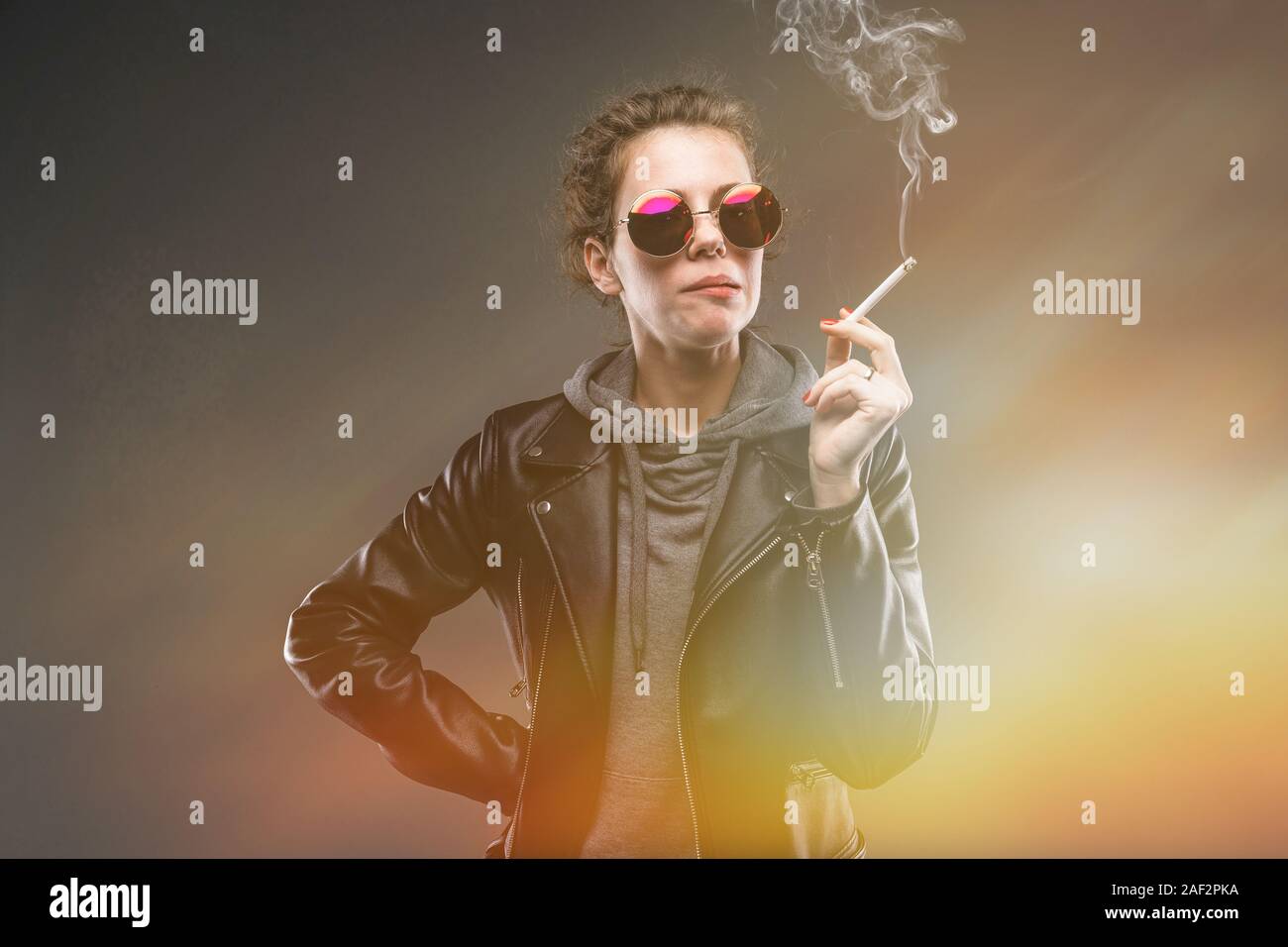 Caucasian girl with rough facial features in a black jacket smokes a ...