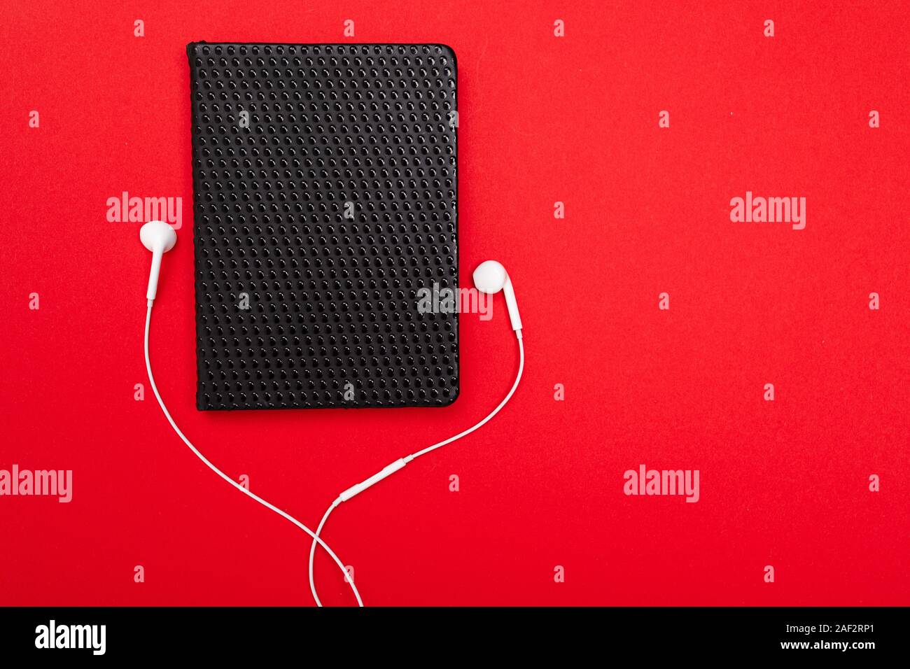 Black notebook with white earphones isolated on red background Stock ...