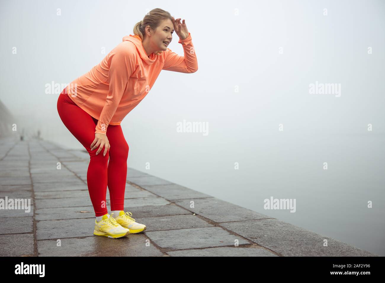 Sporty lady standing bent over on the street Stock Photo - Alamy