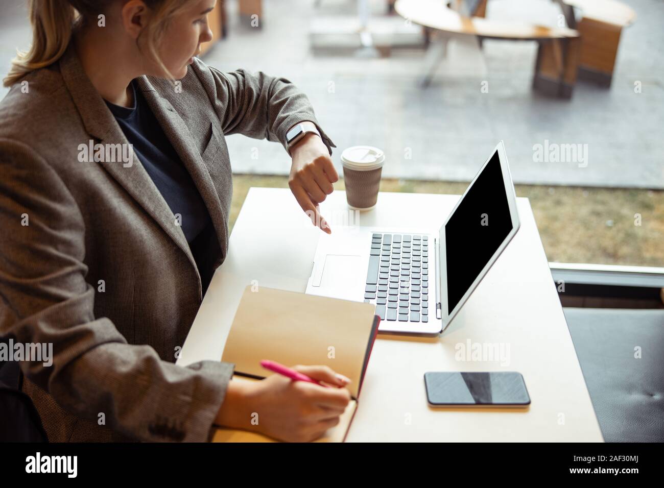 Pretty lady looking at watch while working in cafe Stock Photo - Alamy