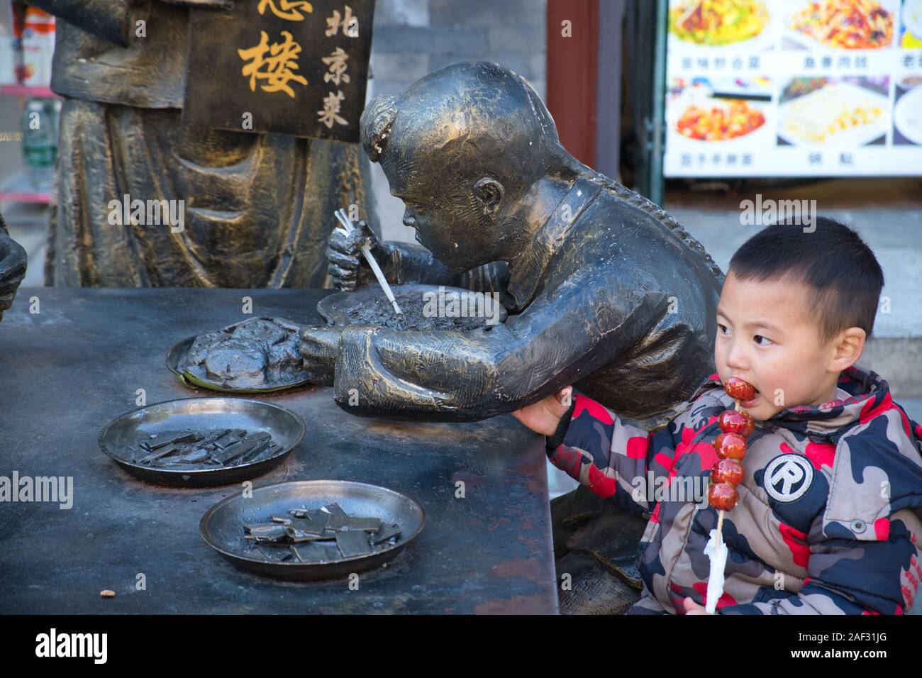 Child sits with historical, statues whilst eating traditional Chinese ...
