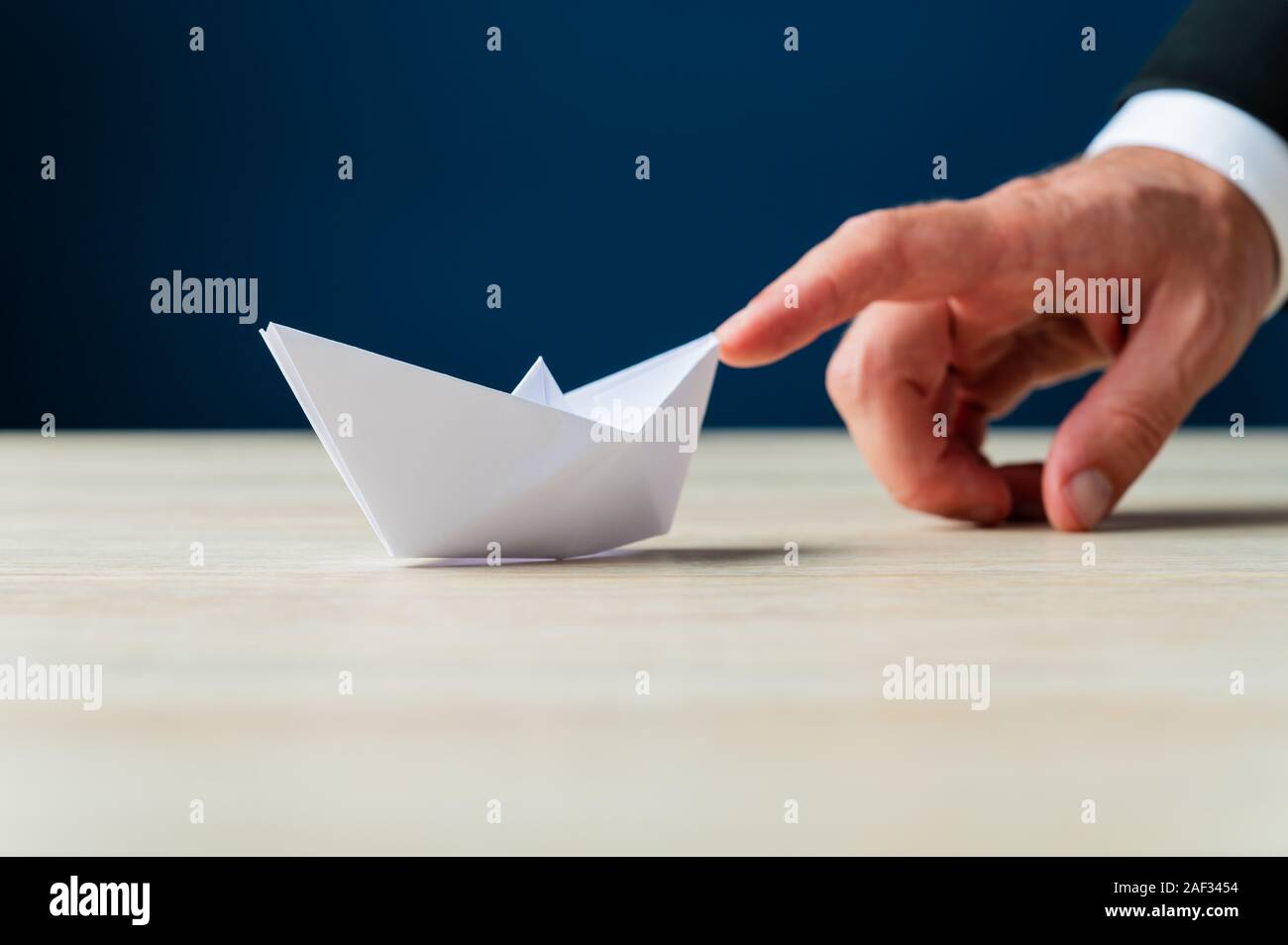 Finger of a businessman pushing forward paper made origami boat in a ...
