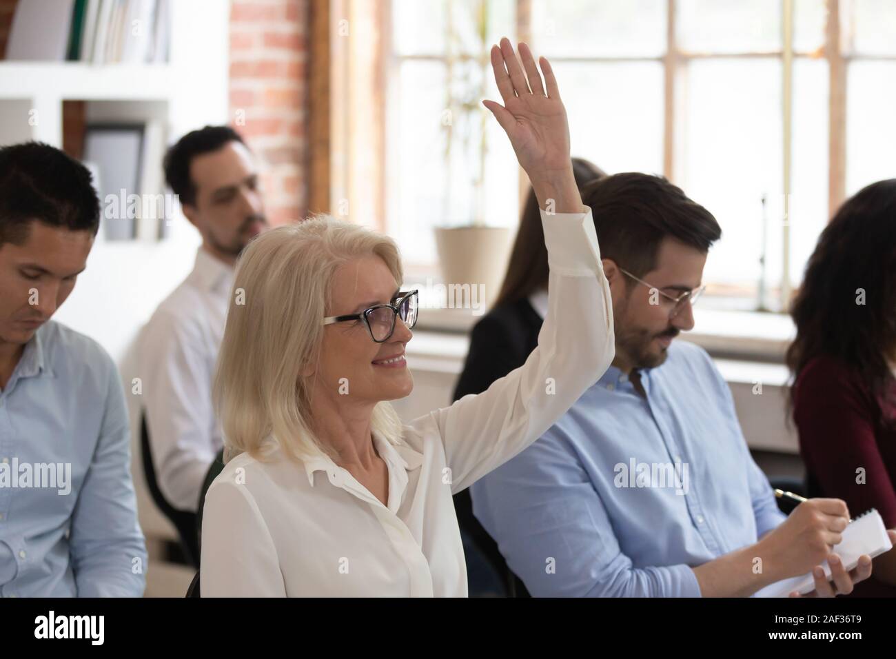 Middle aged woman raising hand to ask question at seminar Stock Photo ...
