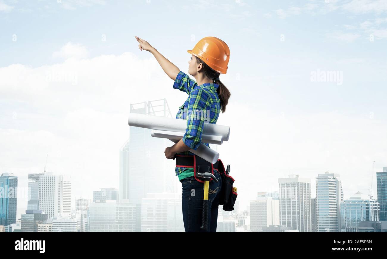 Female engineer in hardhat standing with technical blueprints and ...