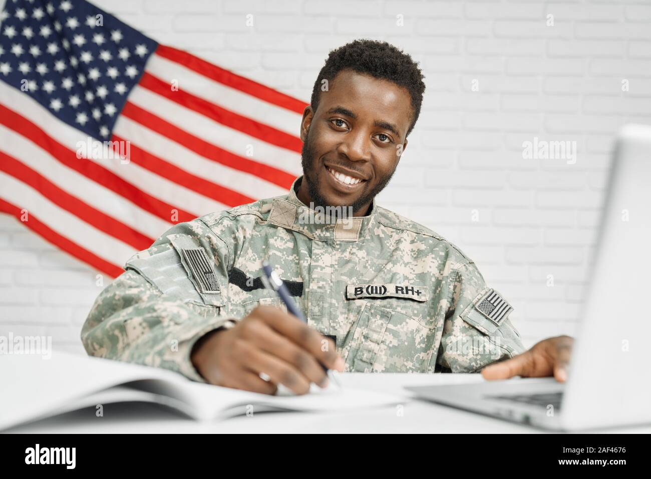 Happy soldier sitting on table at workplace and writing in documents ...
