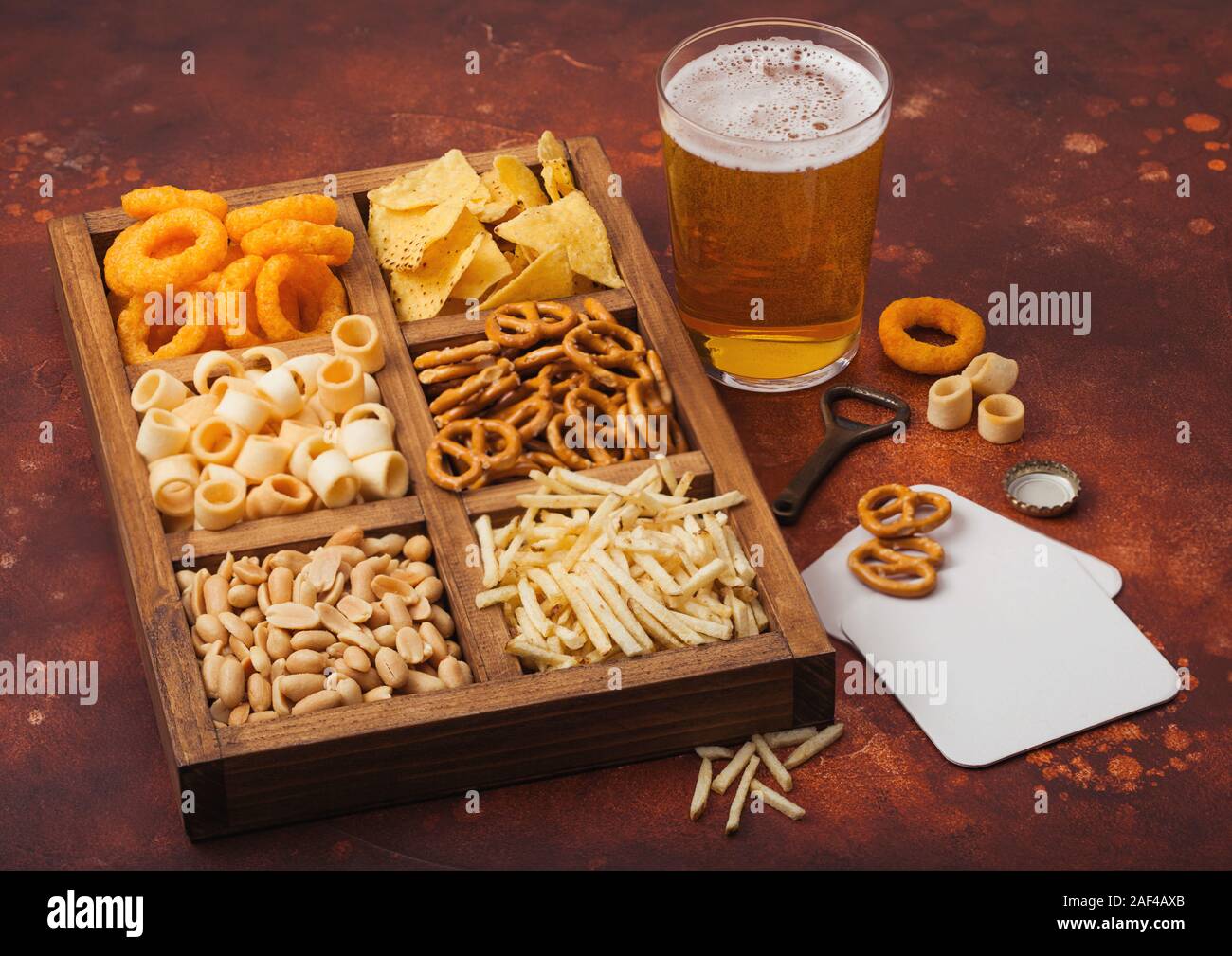Glass of craft lager beer and opener with box of snacks on brown ...