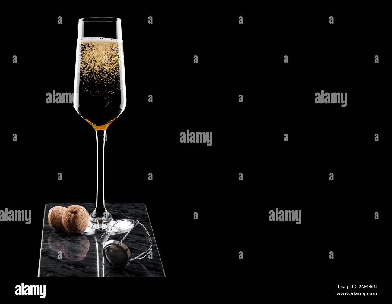 Elegant glass of yellow champagne with cork and wire cage on black ...