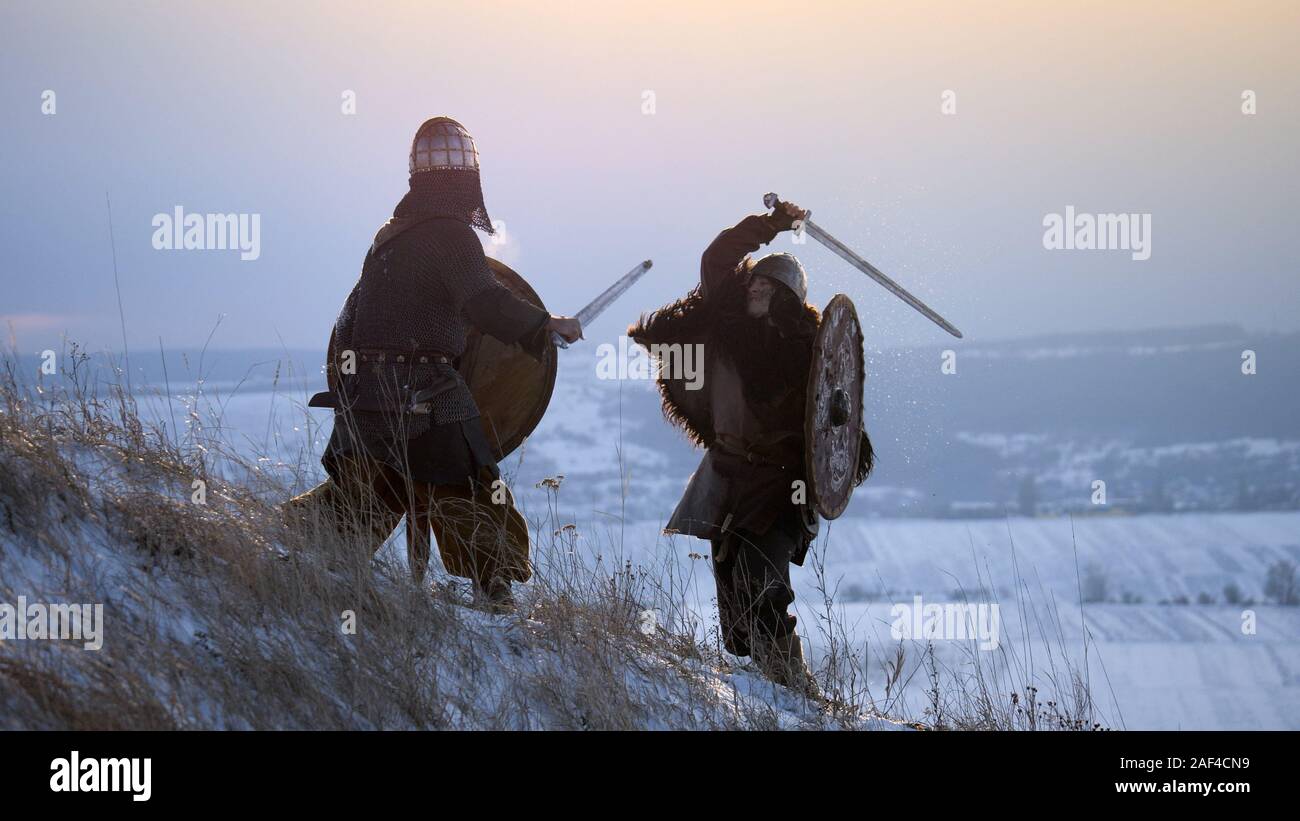Two viking are fighting with axes and shields on the winter meadow ...