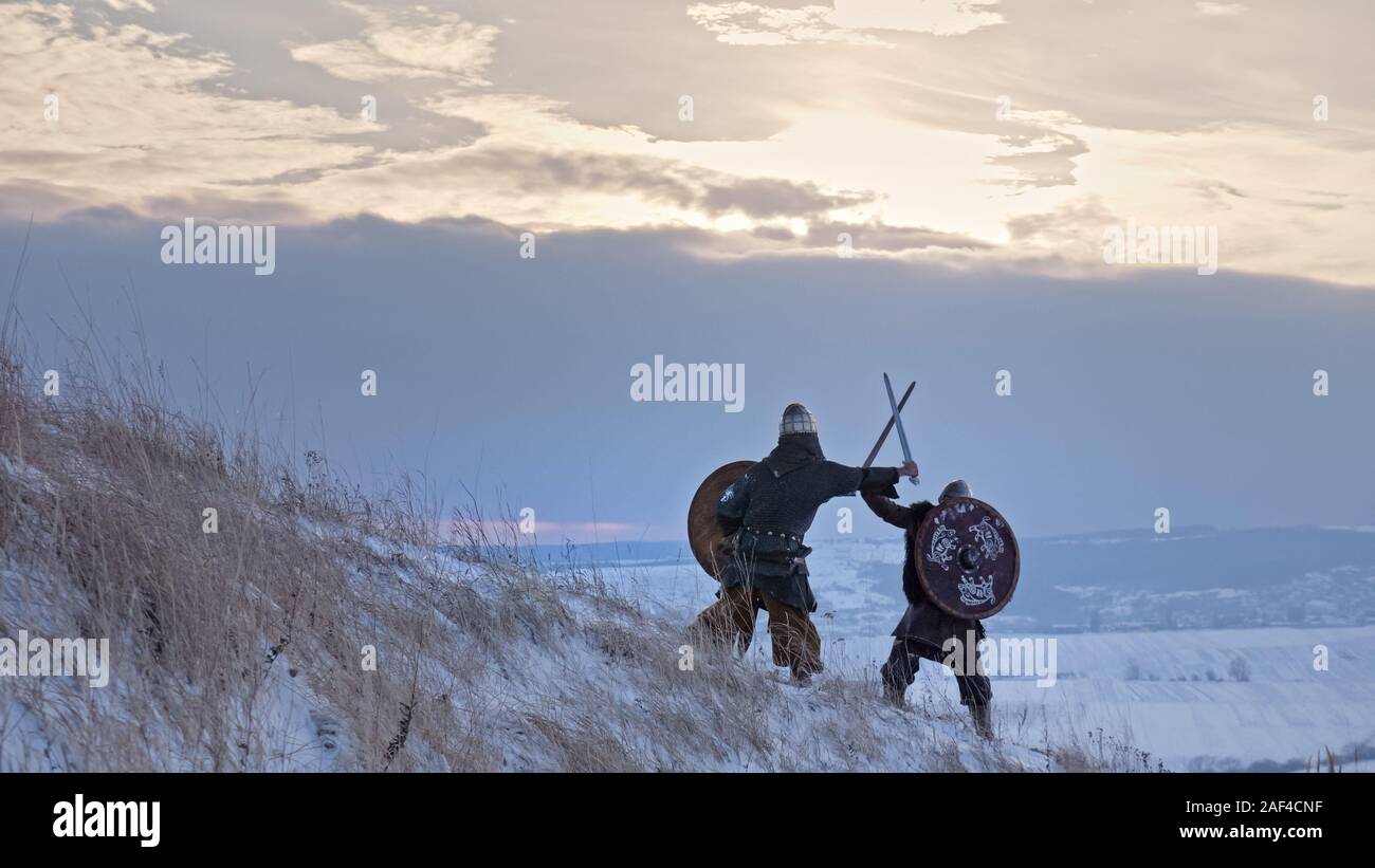 Two viking are fighting with axes and shields on the winter meadow ...