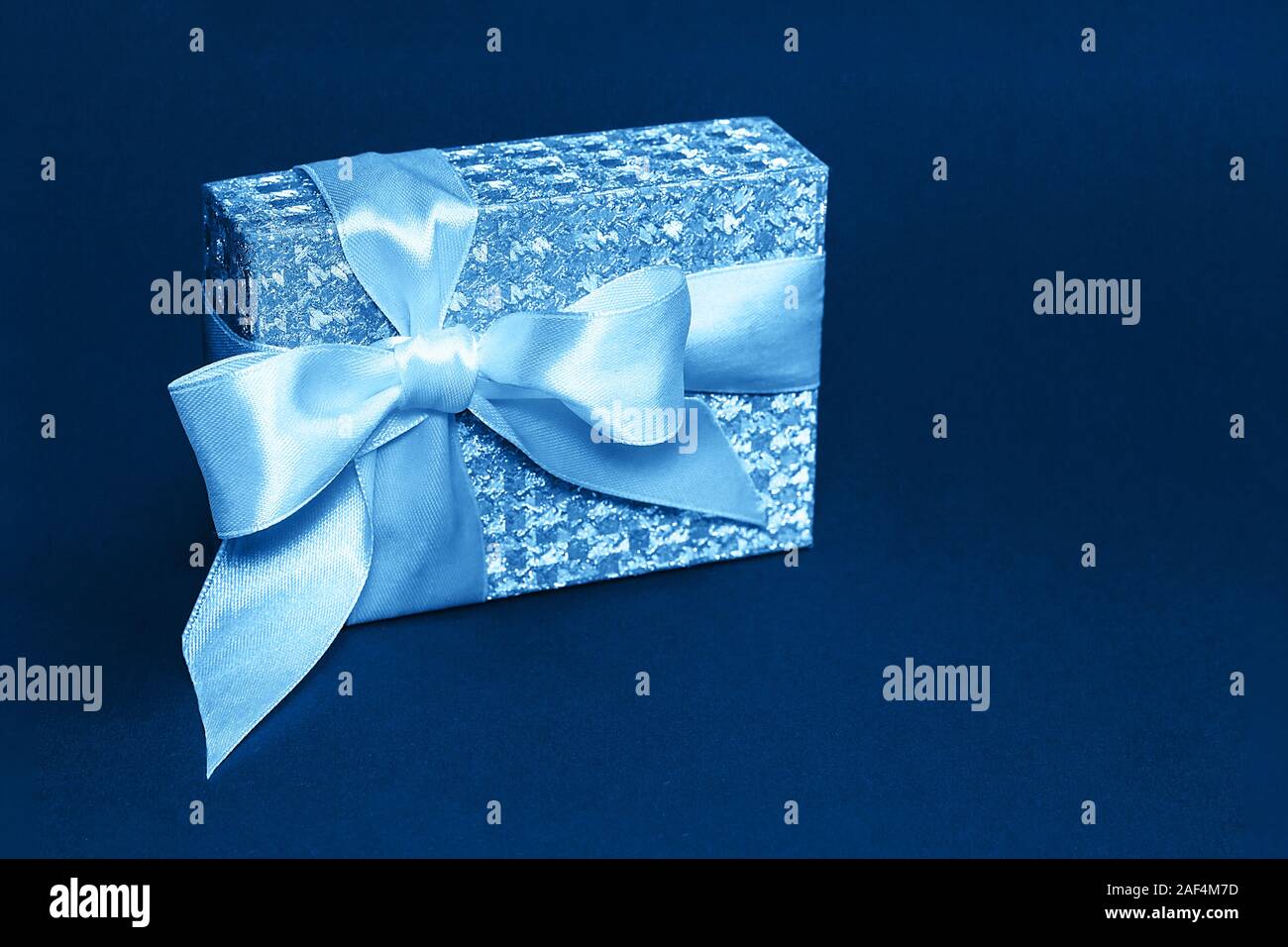 Sparkling shiny present box with a silk bow in trendy blue color ...