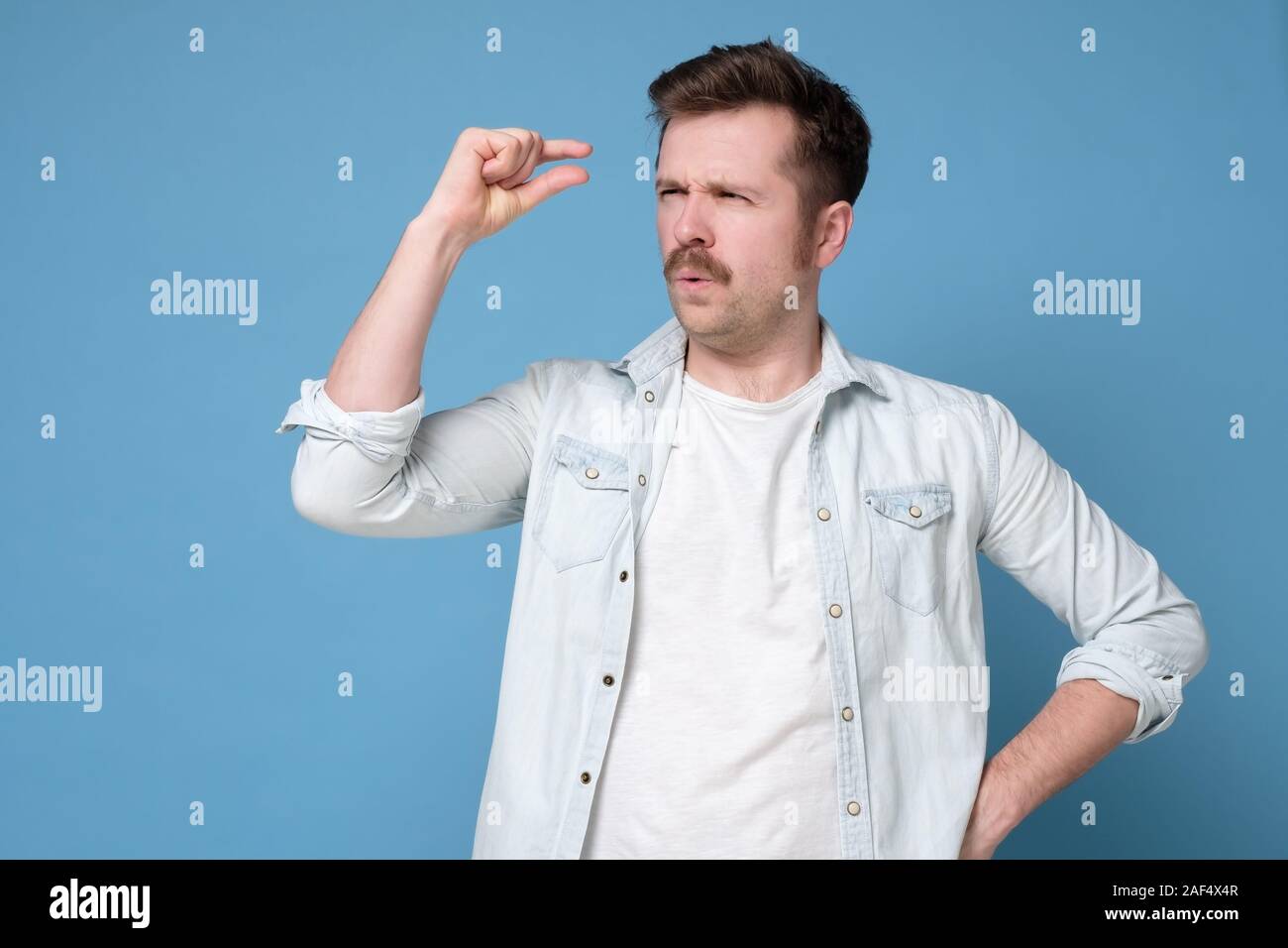 Young caucasian man gesturing with hand showing small size sign with ...