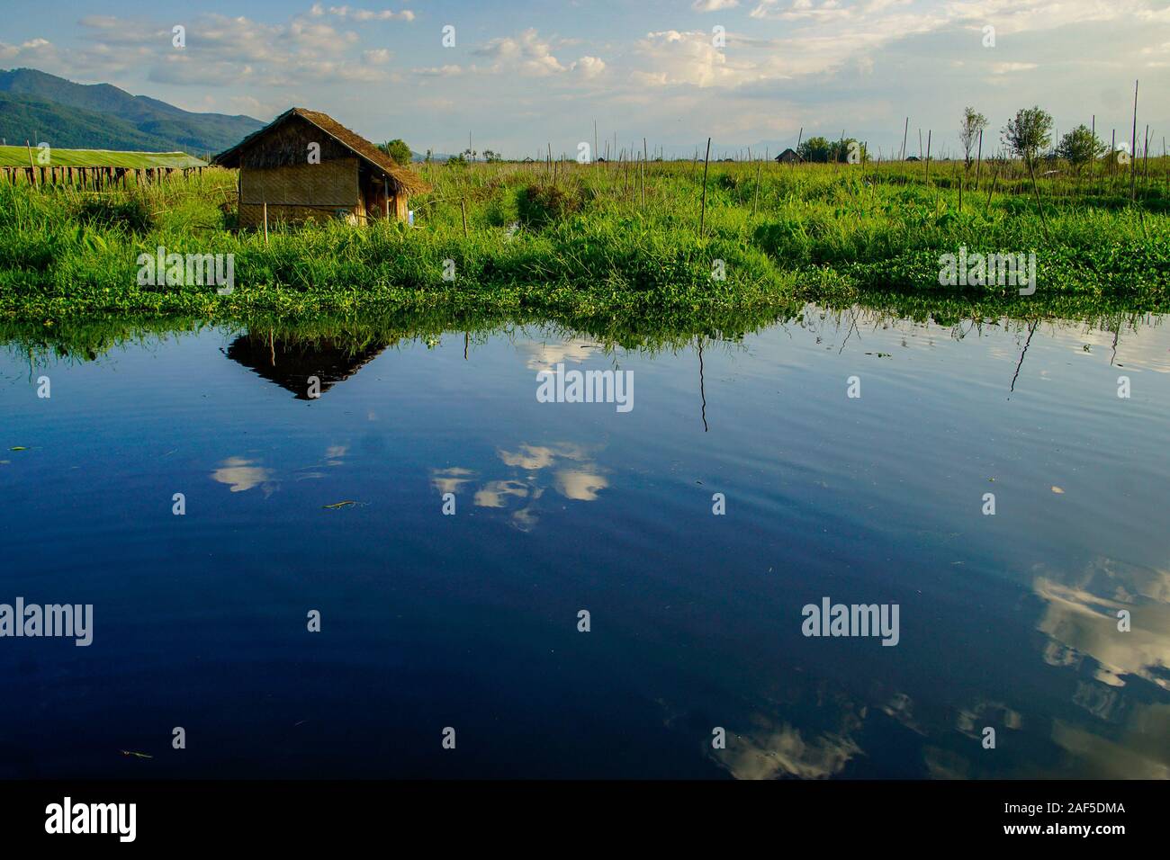 The calm, still waters of Inlay lake reflect the clouds and the blue ...