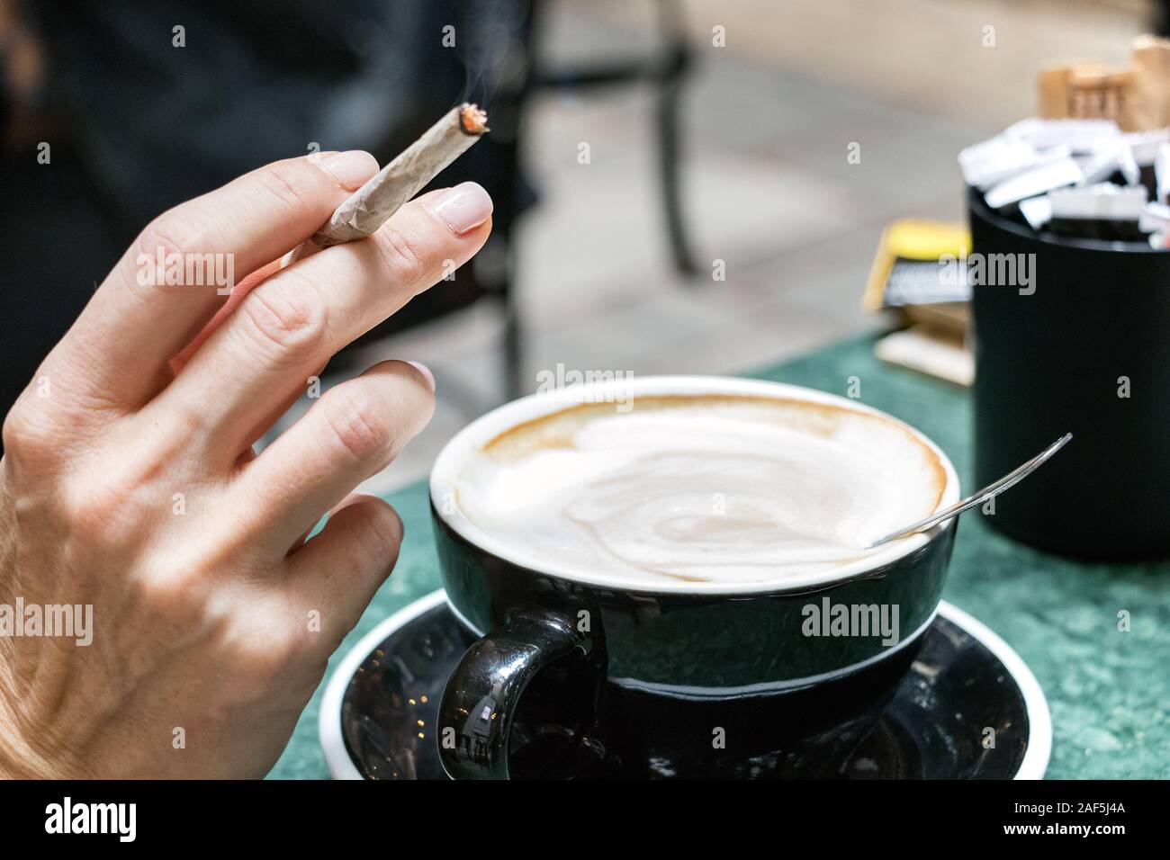 Female hand holding a cigarette having coffee outdoors at a coffee shop ...