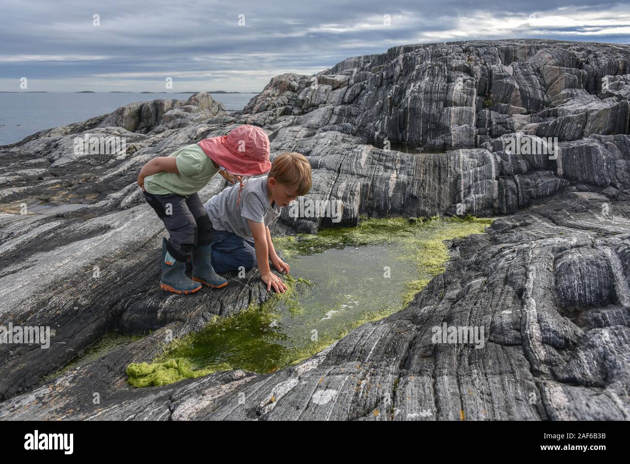 Boy and girl playing between rocks with algae, Straumsholmen, Atlantic ...