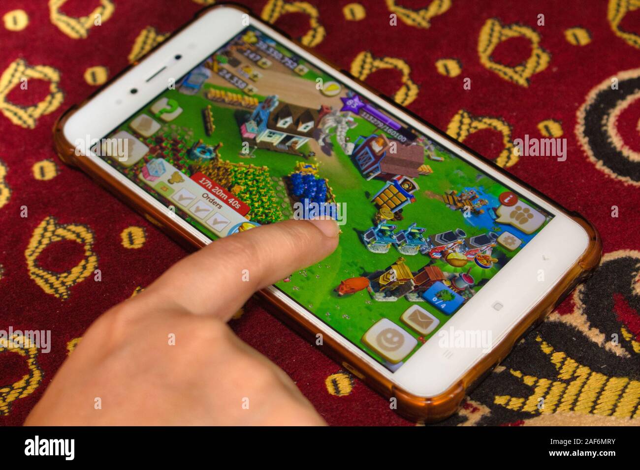 Finger on mobile screen playing a farming mobile game Stock Photo - Alamy