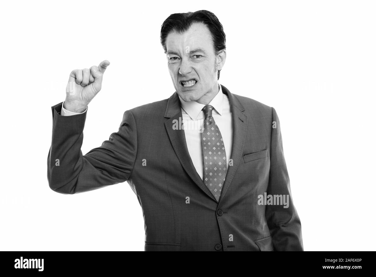 Studio shot of mature businessman looking furious while pointing finger ...