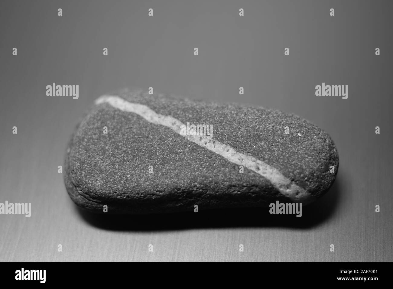 Pebble stone with natural diagonal white line on the table, bw photo ...