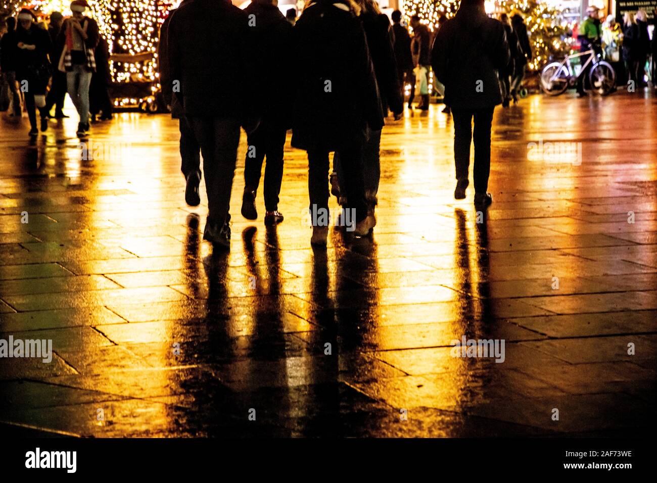 People walk in the evening through a city center, wet underground ...