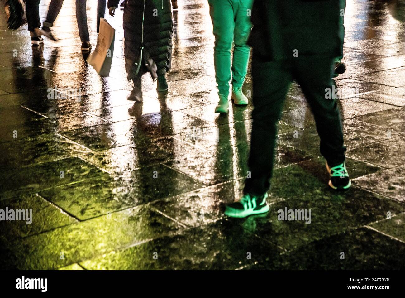 People walk in the evening through a city center, wet underground ...