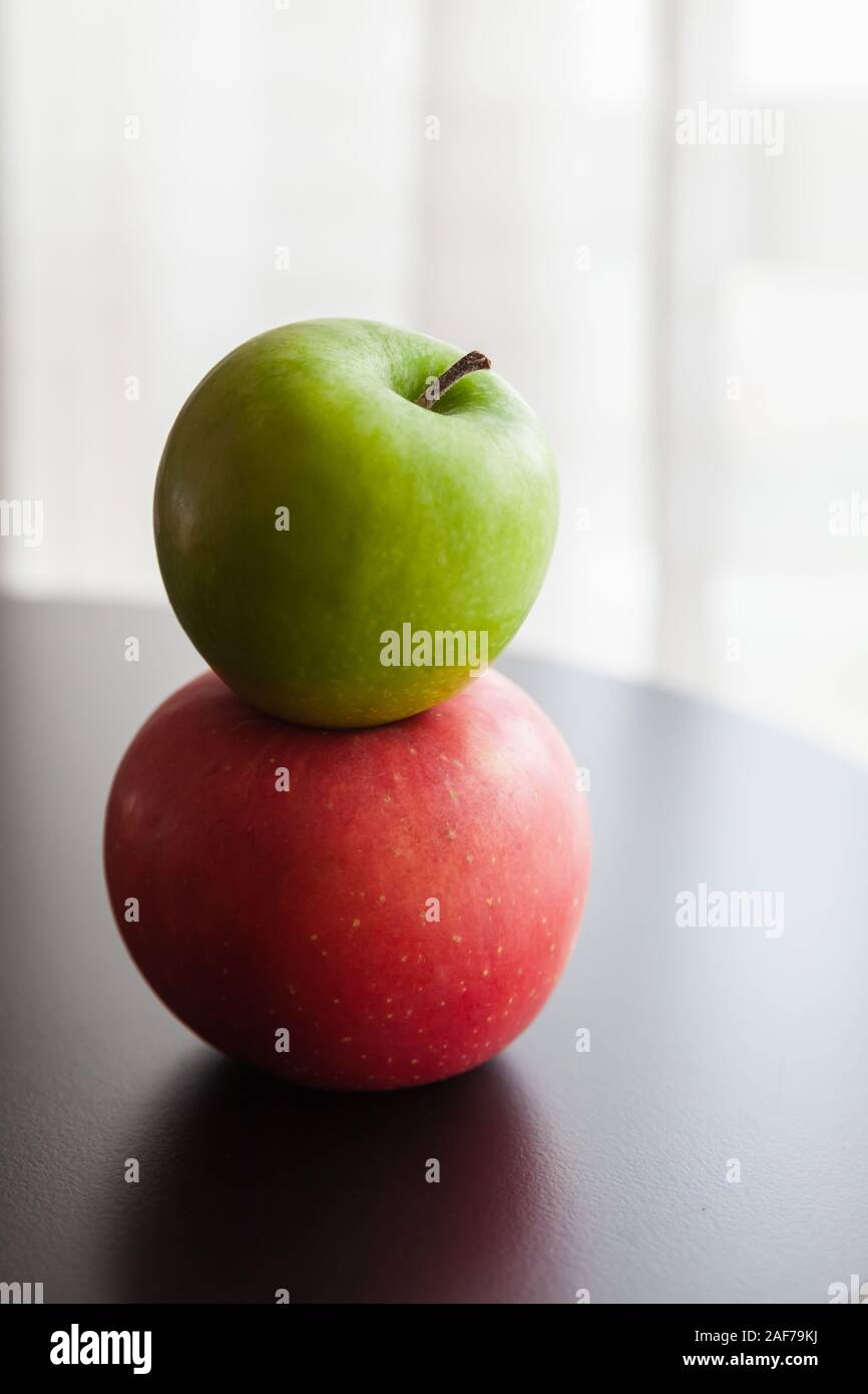 Two apples green and red lay on a round black desk. Close up vertical ...
