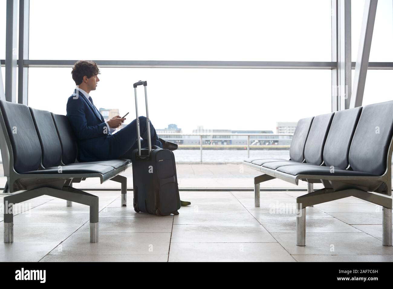 Businessman Sitting In Airport Departure Lounge Using Mobile Phone ...