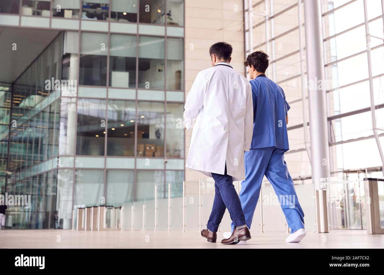 Rear View Of Male Medical Staff Talking As They Walk Through Lobby Of ...