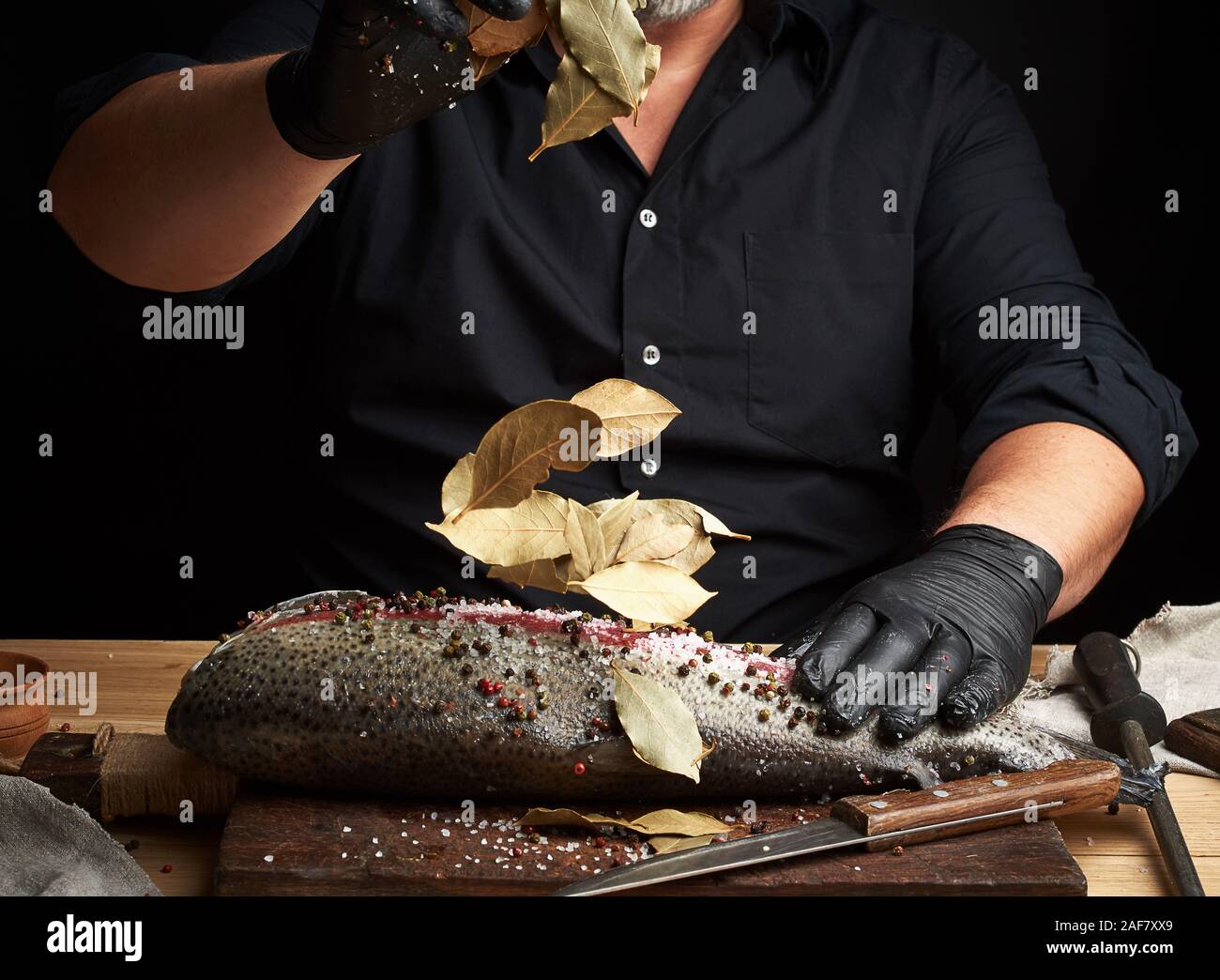 chef in black uniform and black latex gloves pours dry leaves of bay ...