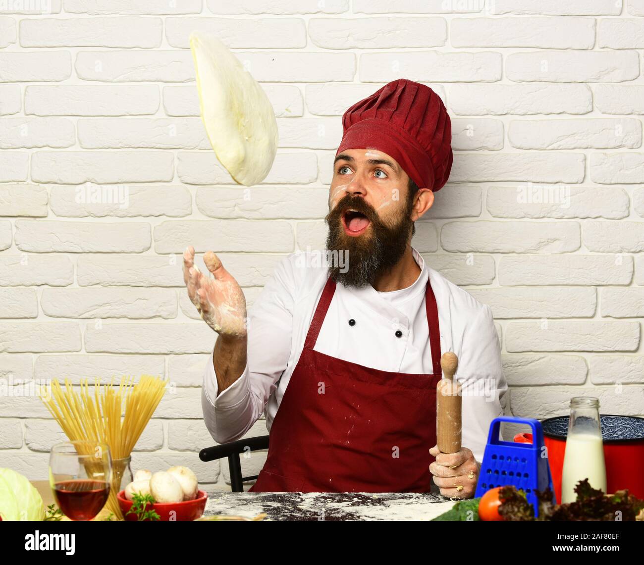 Man with beard throws pizza dough up on white brick wall background ...