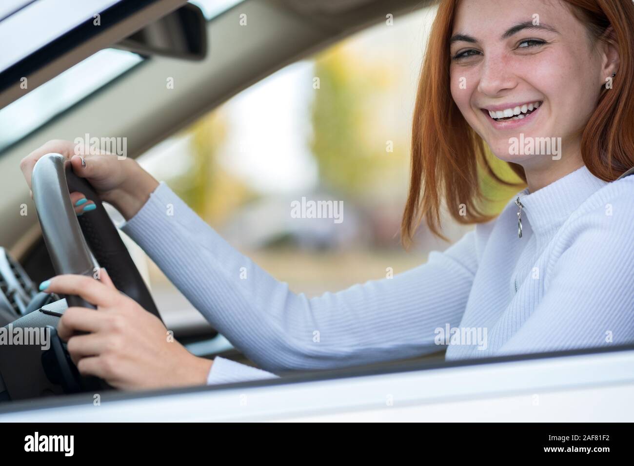 Young redhead woman driver behind a wheel driving a car smiling happily ...