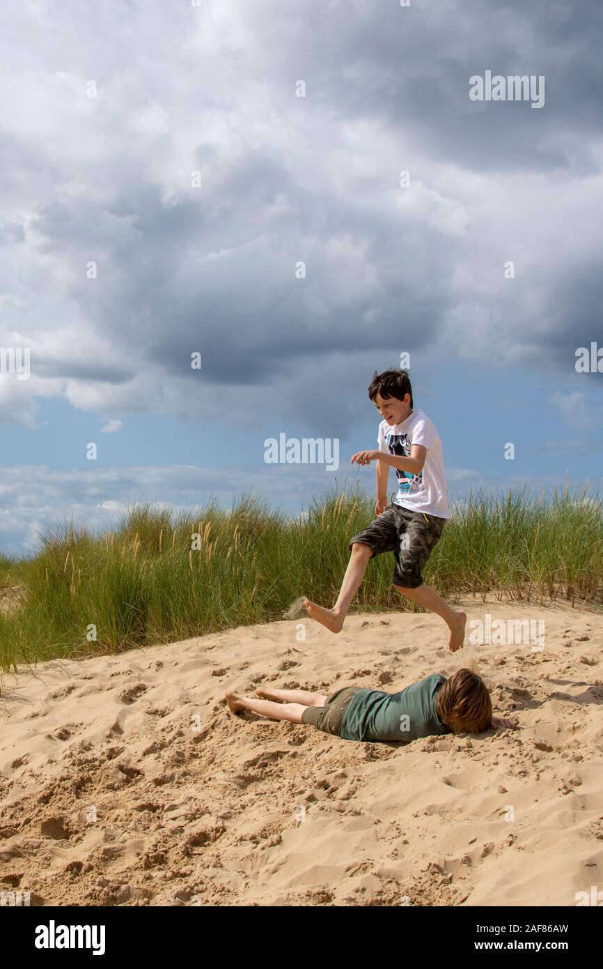 Boys jumping around on sand dune Stock Photo - Alamy