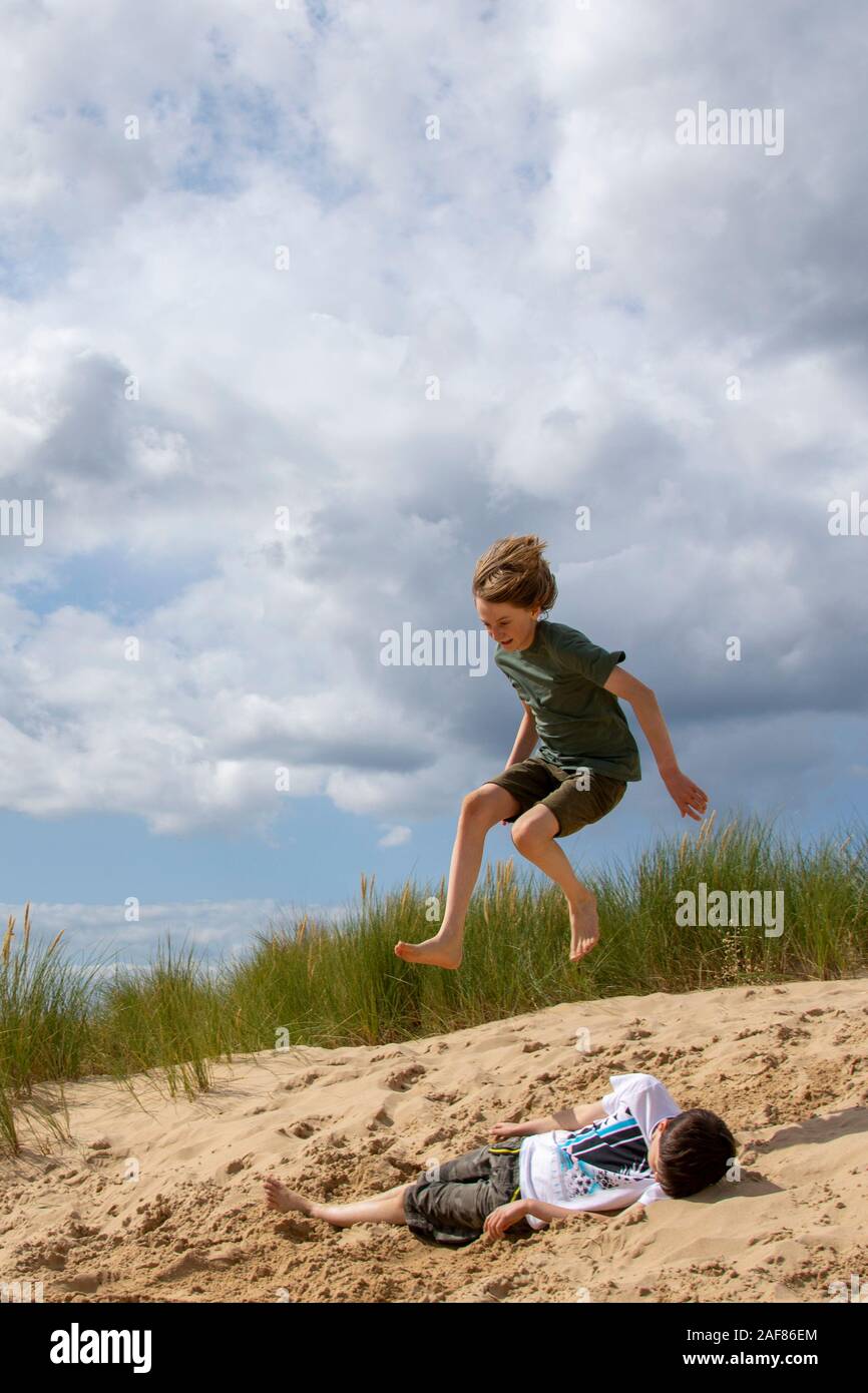 Boys jumping around on sand dune Stock Photo - Alamy