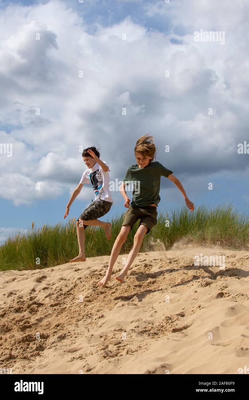 Boys jumping around on sand dune Stock Photo - Alamy