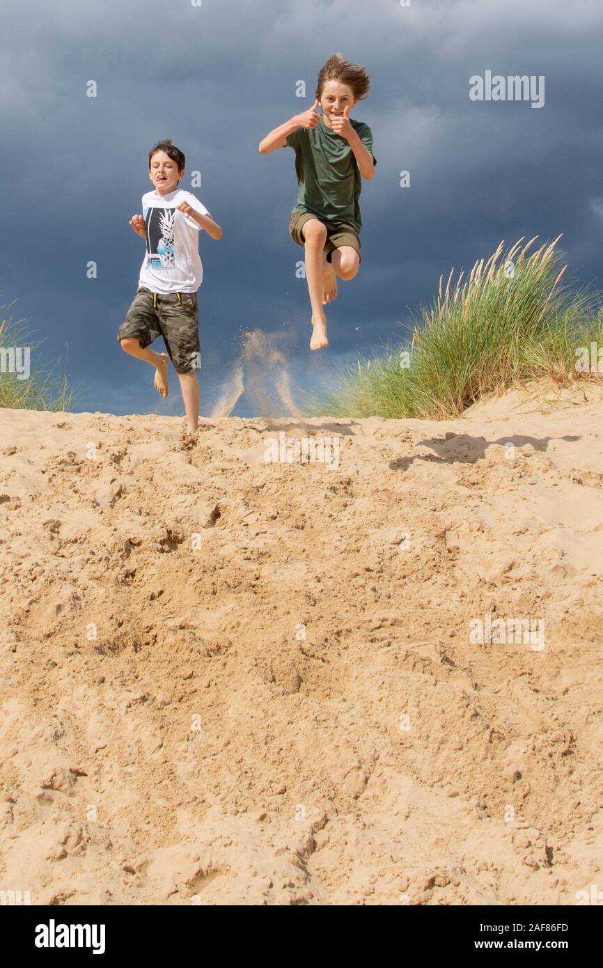 Boys jumping around on sand dune Stock Photo - Alamy