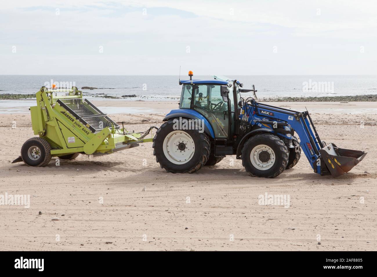 A tractor towing a surf rake to clean debris from a public beach at ...