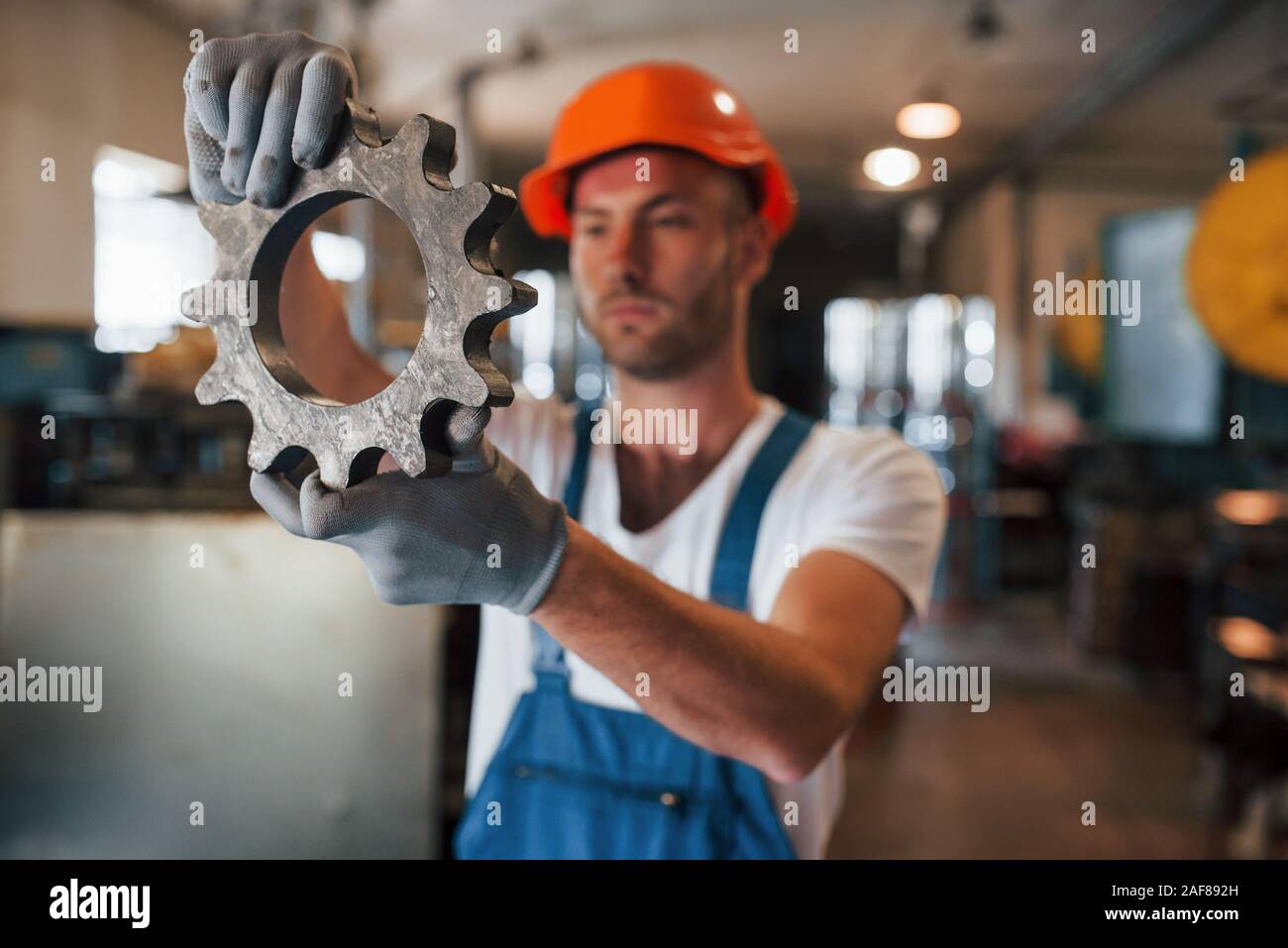 Part of machine. Man in uniform works on the production. Industrial ...