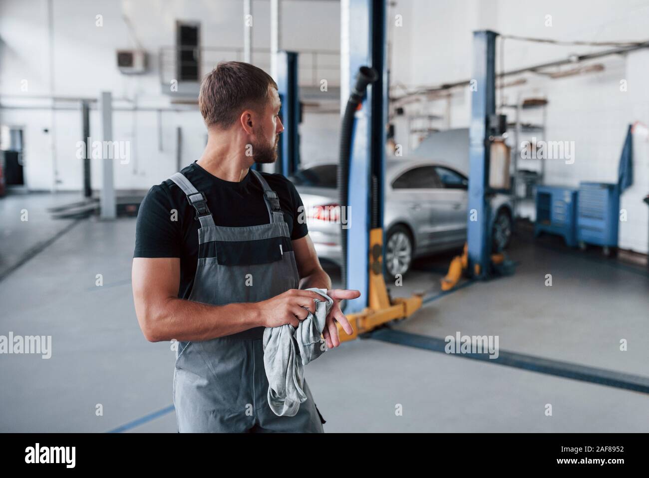 Looks behind. Man in black shirt and grey uniform stands in garage ...