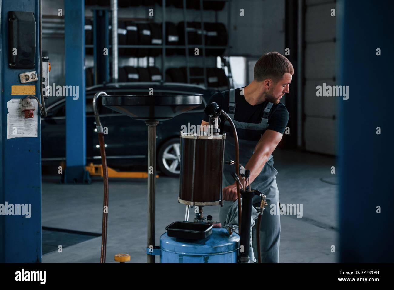 In black shirt and grey uniform. Male mechanic use special device to ...