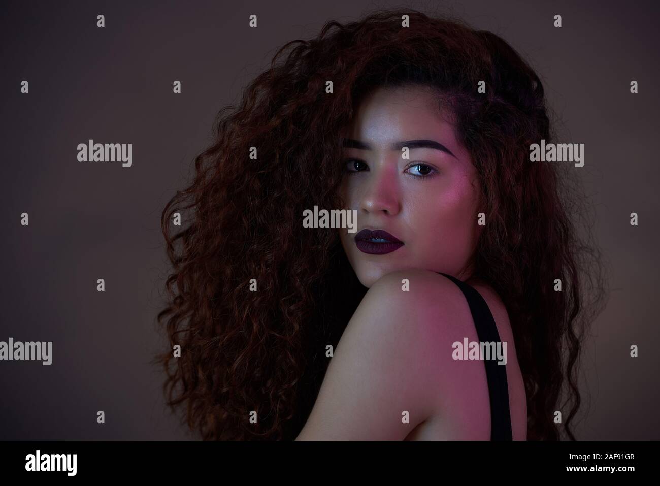 Model with brown curly hair on dark studio background Stock Photo - Alamy