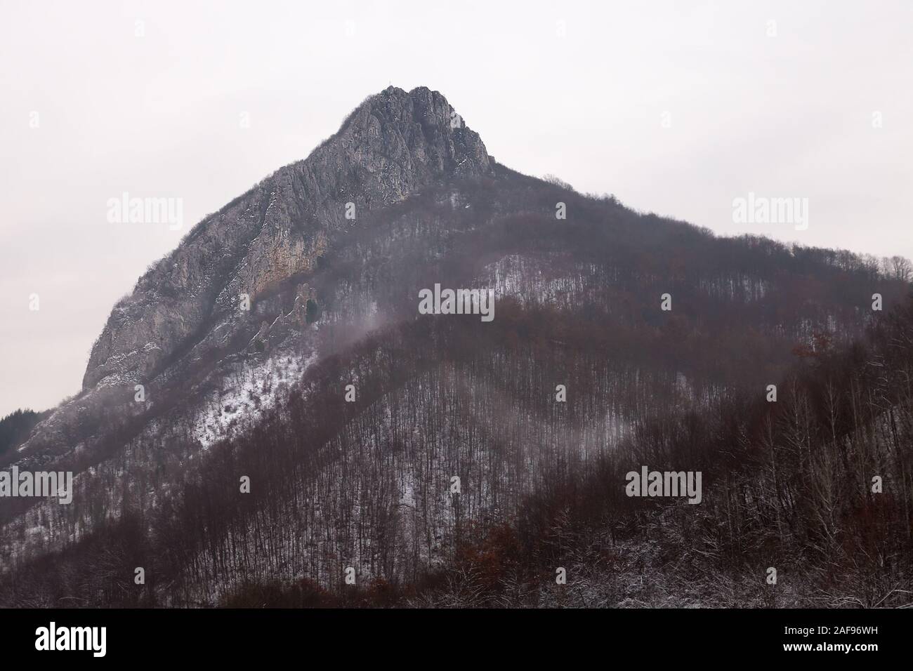 Soft, misty, moody view of a pointy, rocky mountain peak covered by ...
